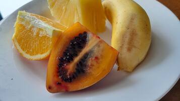 Um prato branco com frutas cortadas, incluindo mamão, laranja e manga, sobre uma mesa de madeira.