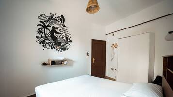 Quarto com cama, decoração na parede, porta e prateleira com objetos.