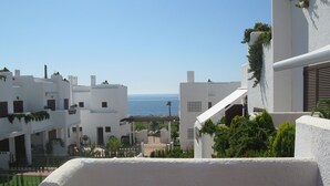 Zona residencial costeira com edifícios brancos, vista clara para o mar e portão fechado.