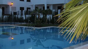 Piscina com o reflexo de um edifício e palmeiras.