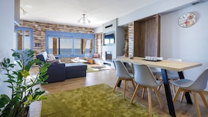 Uma sala de estar moderna com sofá, mesa de jantar com cadeiras, tapete verde e uma grande janela com vista.