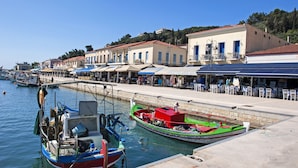 Uma marina com barcos atracados, um calçadão à beira-mar e edifícios com portas e toldos azuis.