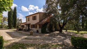 Uma casa rústica com um caminho de pedra que leva a uma mesa e cadeiras de madeira, cercada por vegetação e árvores.