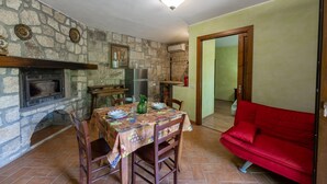 Uma sala de jantar com parede de pedra, lareira, sofá vermelho e piso ladrilhado.