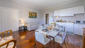 Uma cozinha moderna com armários brancos, micro-ondas e uma sala de jantar com mesa posta para quatro pessoas.
