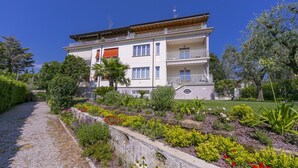 Um edifício com vários andares e varandas, cercado por um jardim bem cuidado com diversas plantas e flores.