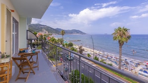 Uma varanda com vista para a praia, área de estar externa e céu claro.