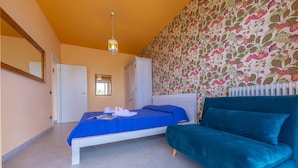 Um quarto com cama, sofá azul, guarda-roupa e papel de parede floral.