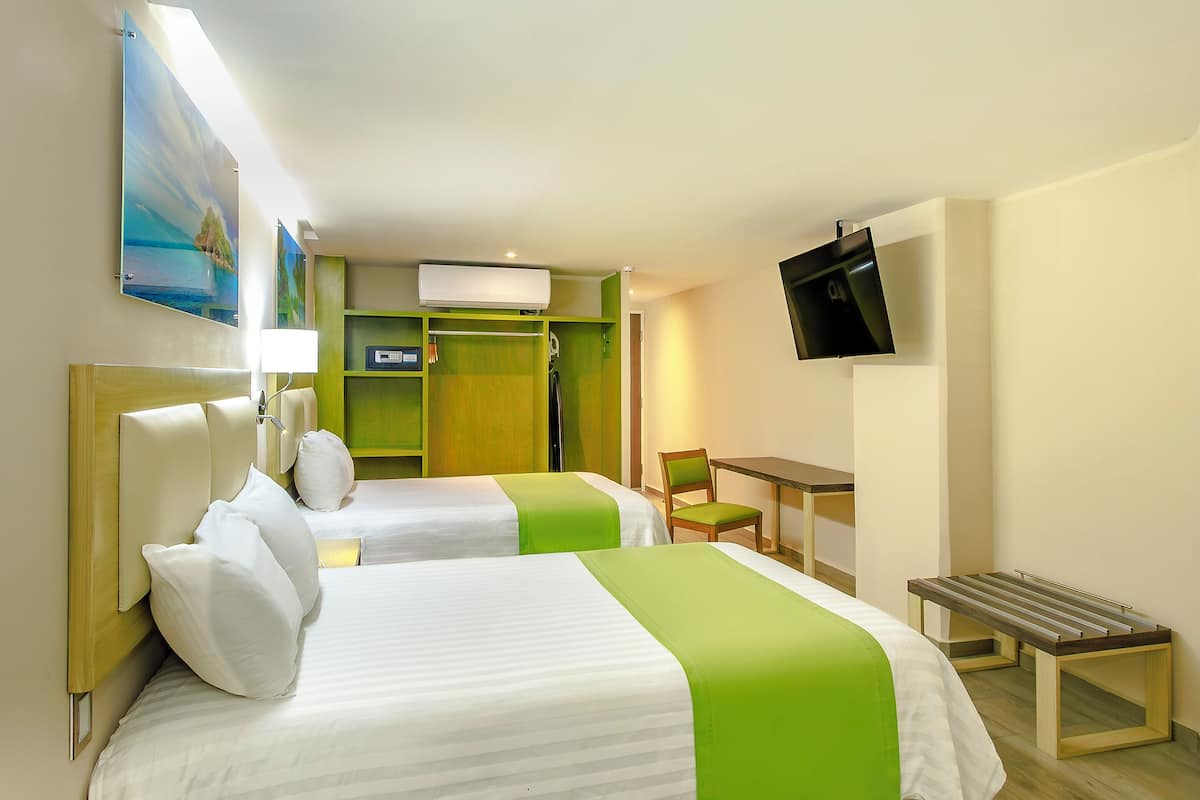 Quarto de hotel com duas camas, uma escrivaninha, uma cadeira, uma televisão e um guarda-roupa.