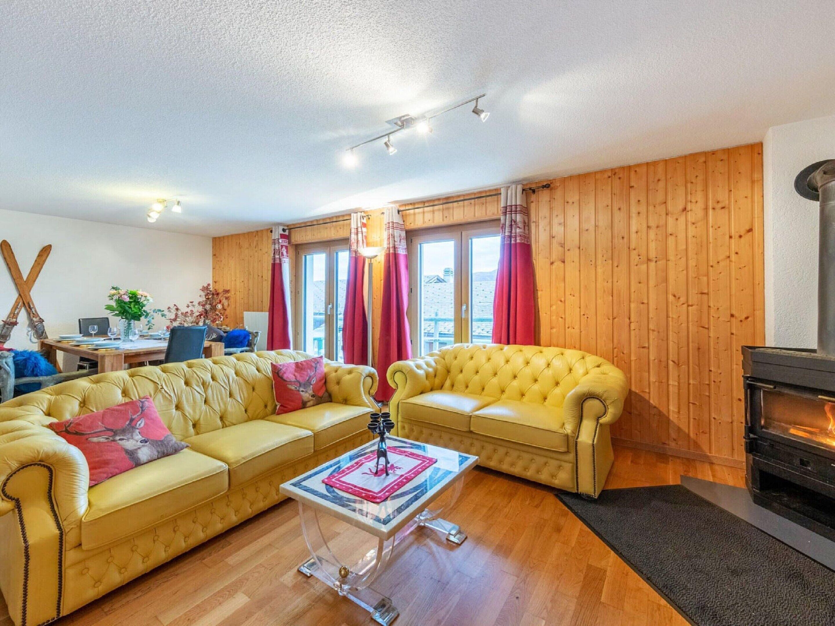 Uma sala de estar aconchegante com dois sofás amarelos, uma mesa de centro de vidro transparente e uma lareira.