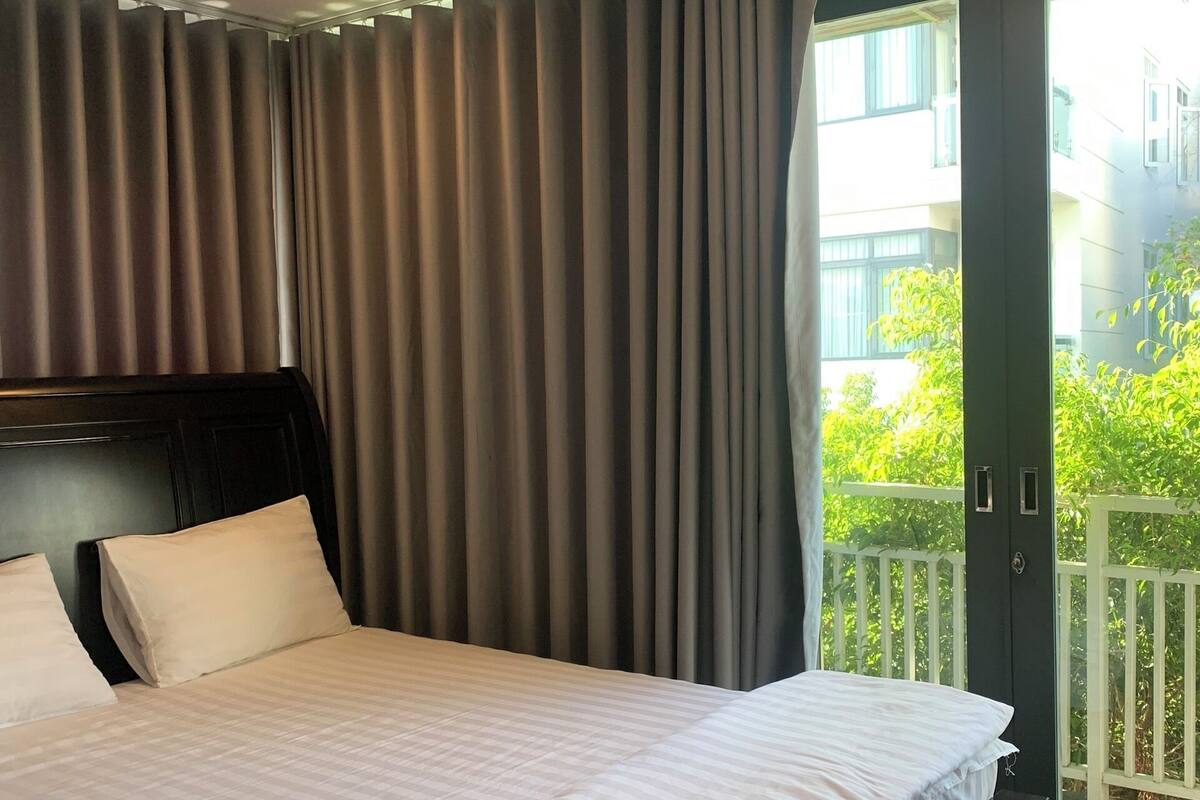 Quarto de hotel com uma cama grande, cabeceira escura e vista para o verde através de uma porta de vidro deslizante.