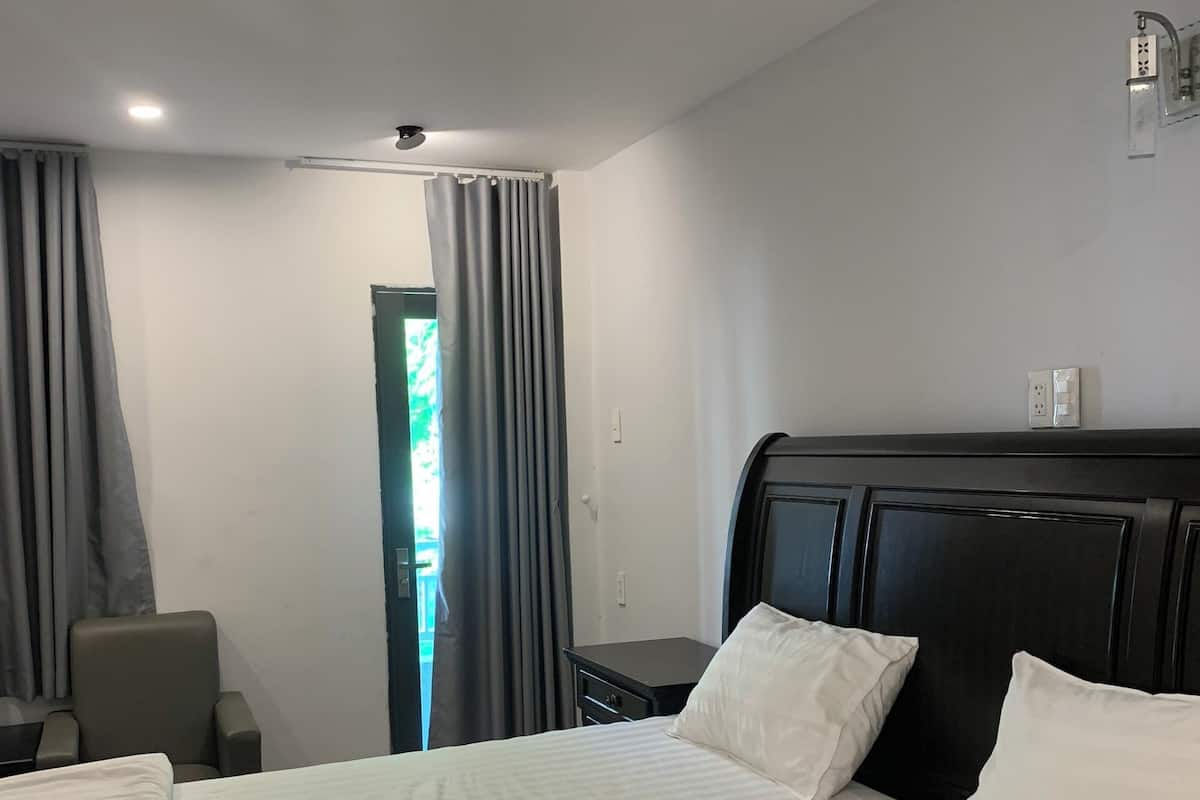 Quarto de hotel com uma cama, uma cadeira, uma escrivaninha e uma janela com cortinas.
