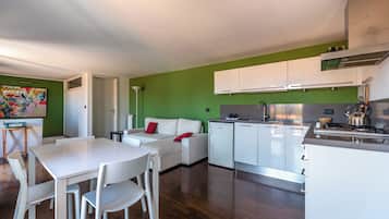 Cozinha moderna com armários brancos, área de refeições com mesa e cadeiras brancas, e uma parede de destaque verde.