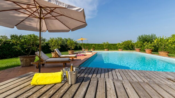 Um deck de madeira com cadeiras de descanso e piscina.