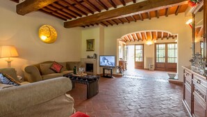Uma sala de estar ampla, com lareira, televisão e uma grande janela com vista para um jardim.