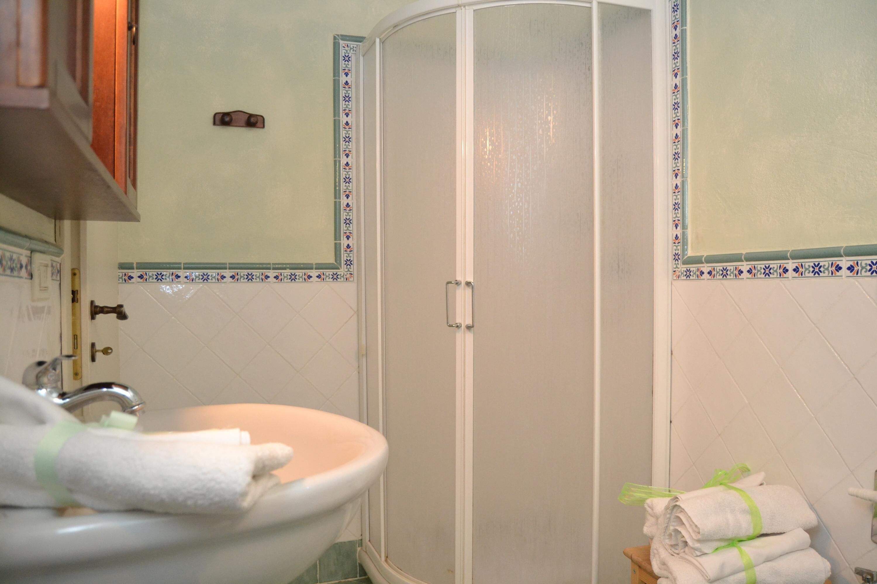 Um banheiro com pia, chuveiro com porta de vidro e porta-toalhas.