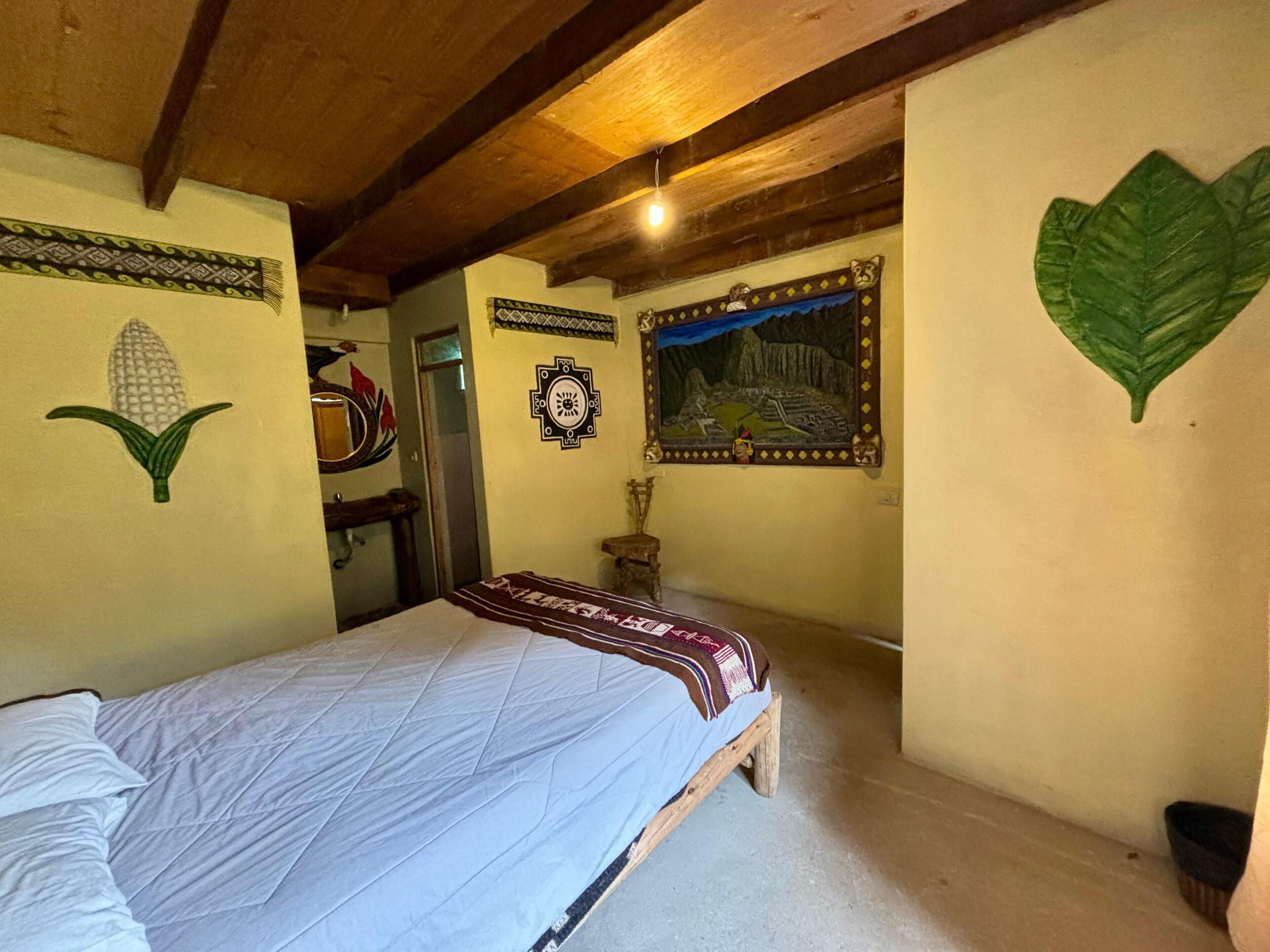 Quarto com cama, teto de madeira, parede com pintura e um enfeite de folha verde.