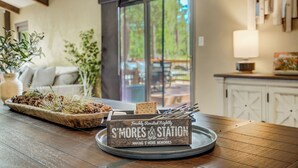 Uma mesa de jantar com uma bandeja de lanches, uma caixa com a inscrição "S'mores Station" e vista para um pátio com porta de correr de vidro.