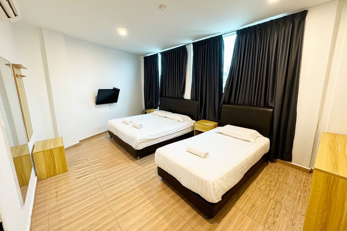 Quarto de hotel com duas camas, uma TV de tela plana na parede e uma janela grande com cortinas escuras.