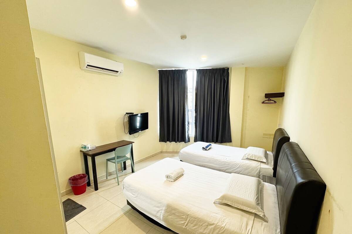 Quarto de hotel com duas camas, uma escrivaninha, uma cadeira, uma televisão e um aparelho de ar condicionado.