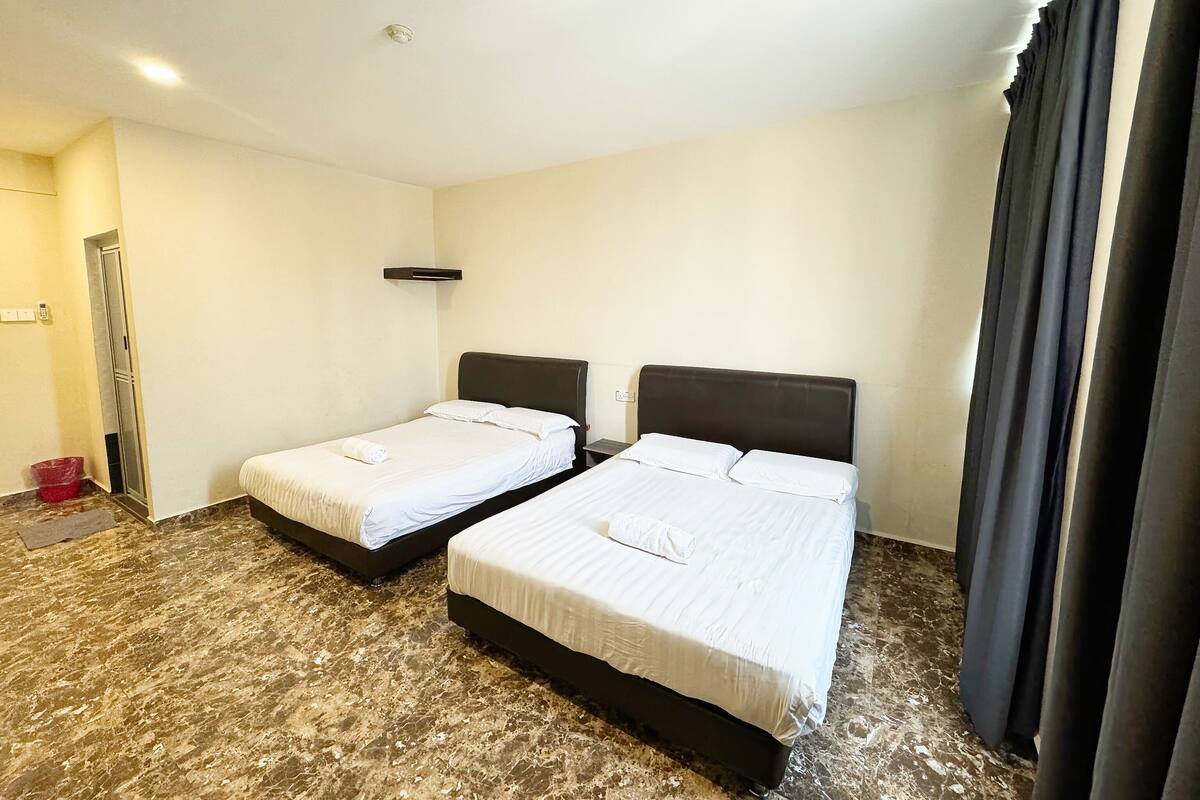 Quarto de hotel com duas camas, piso de mármore, uma mesinha e uma porta.
