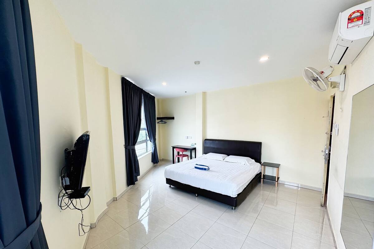 Quarto de hotel com cama, escrivaninha, cadeira, ar condicionado e janela com cortinas.