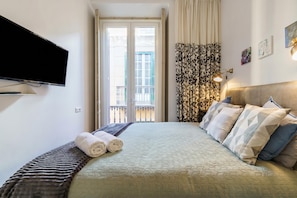 Quarto de hotel com cama, televisão, varanda e janela com cortinas.