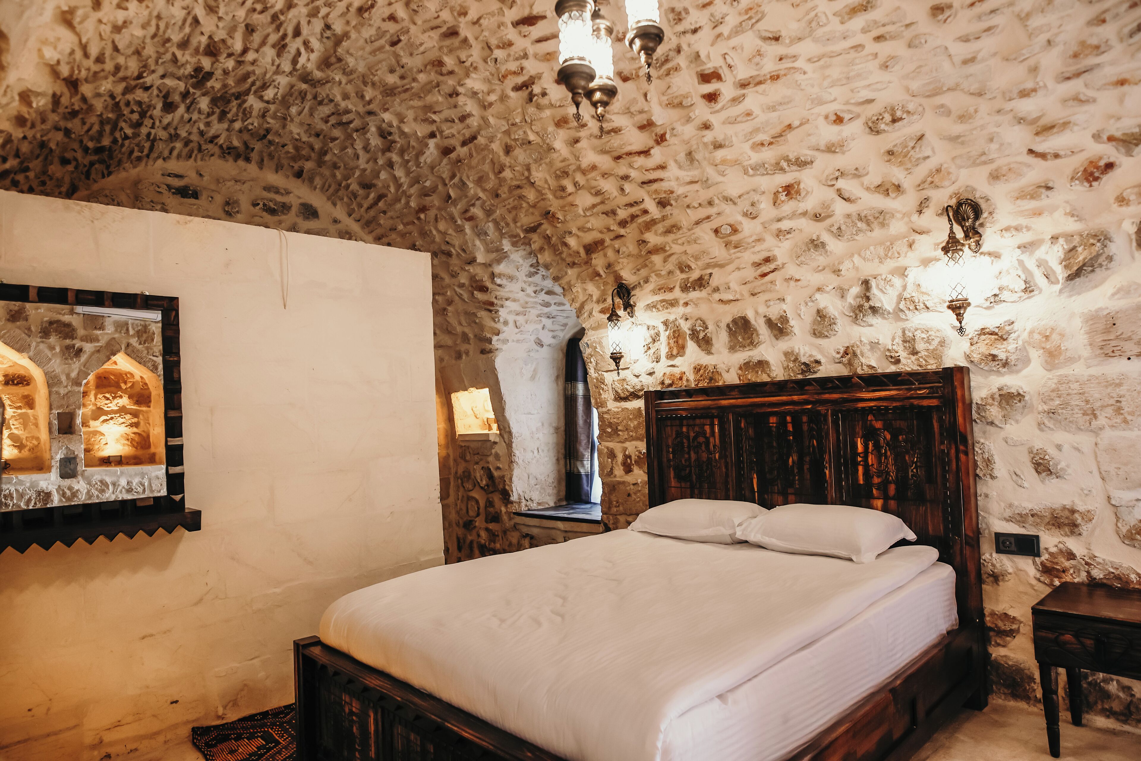 Quarto com teto de pedra, cama de madeira e mesa de cabeceira.