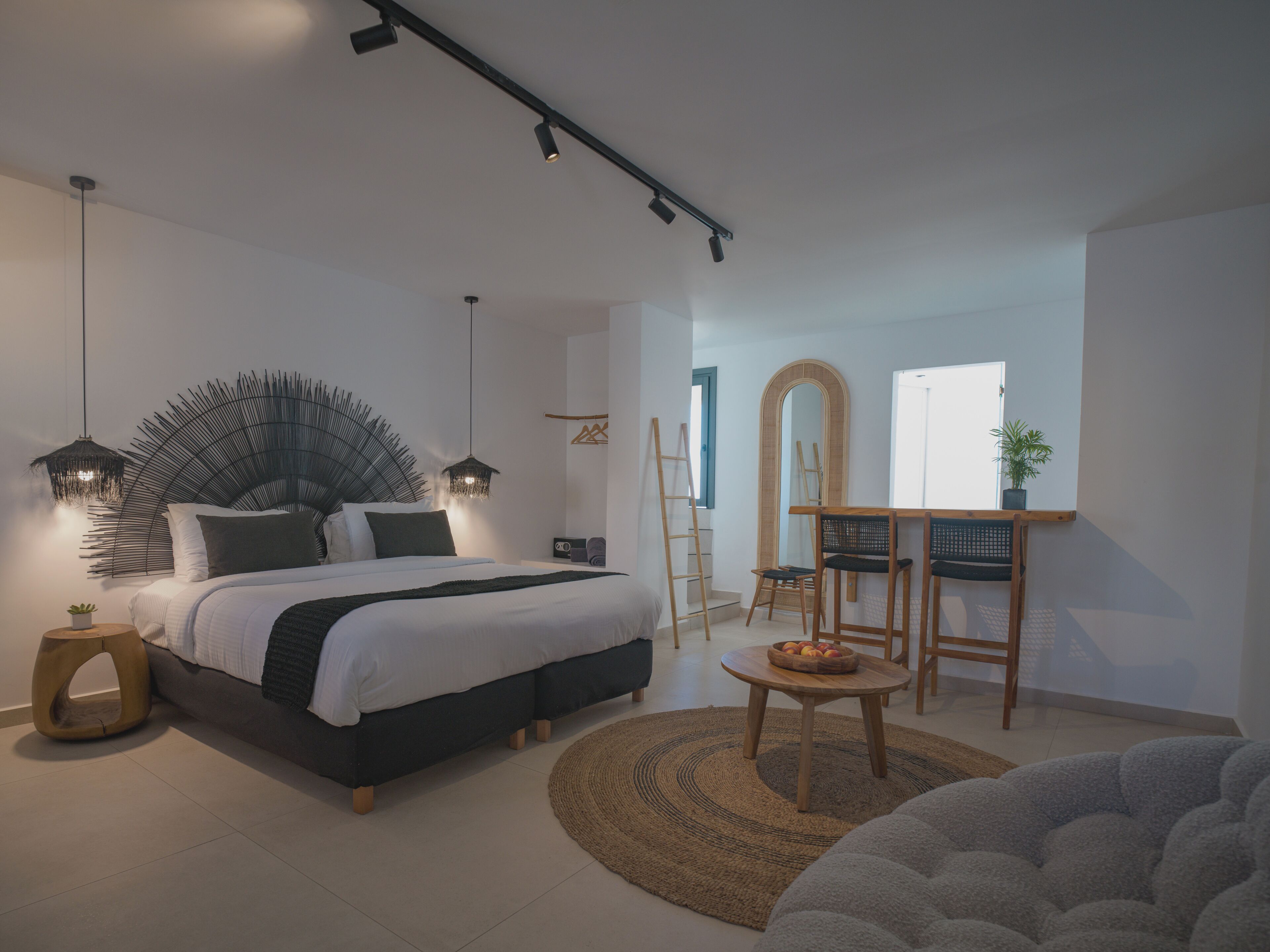 Quarto moderno com cama, luminárias de cabeceira, escrivaninha com cadeiras e um espelho grande.