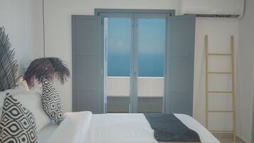 Quarto com cama, vista para o mar através de uma porta deslizante, escada e aparelho de ar condicionado.