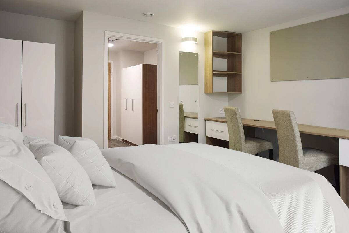Quarto de hotel com cama, escrivaninha, cadeira, guarda-roupa e espelho.