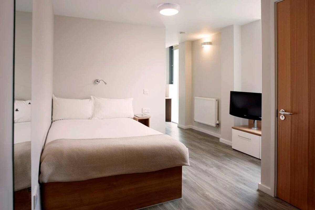 Quarto moderno com cama grande, mesa de cabeceira, televisão e porta de madeira.