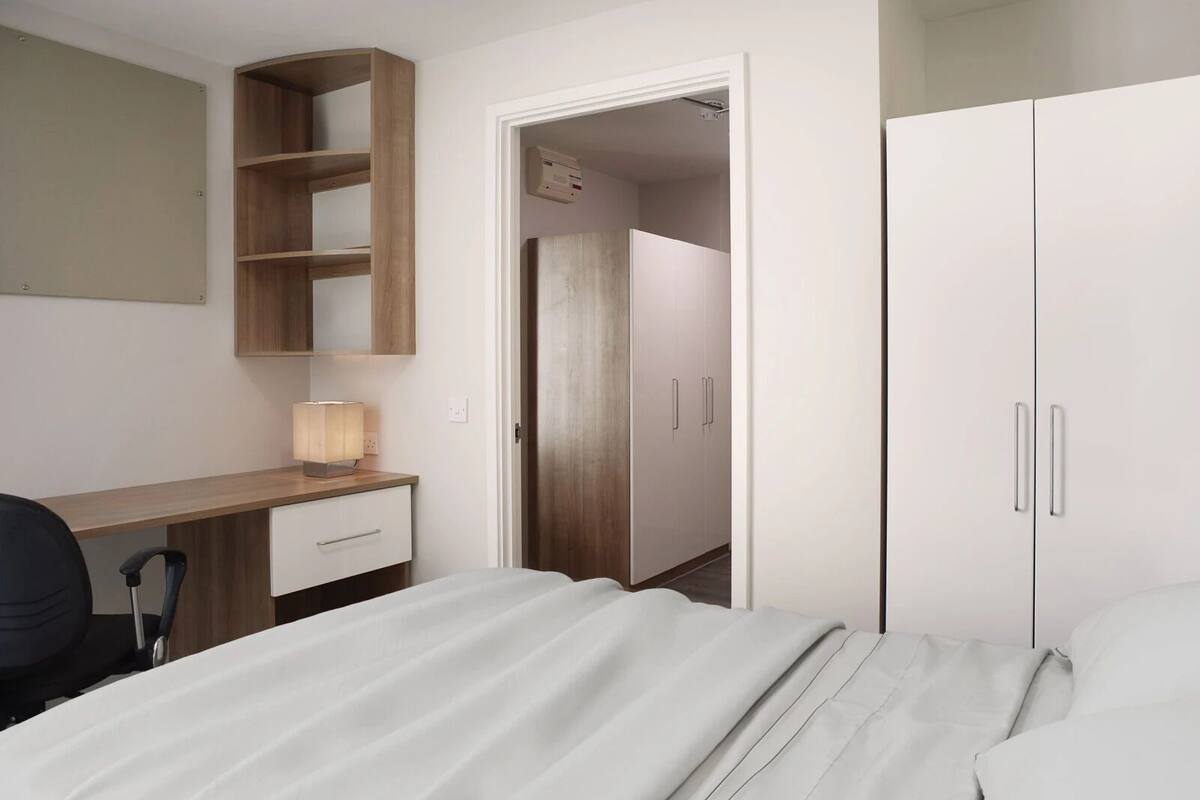 Quarto com uma cama, escrivaninha, cadeira, guarda-roupa e espelho.