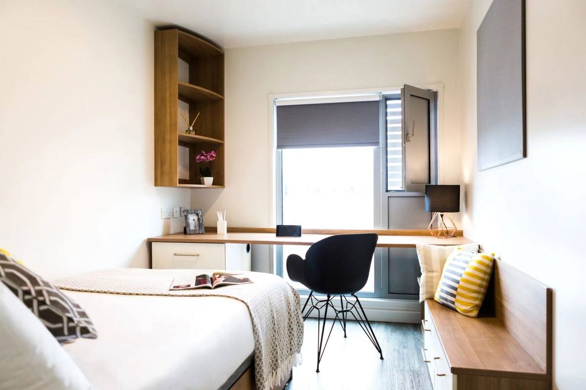 Quarto de hotel moderno com cama, escrivaninha, cadeira e janela com persianas.