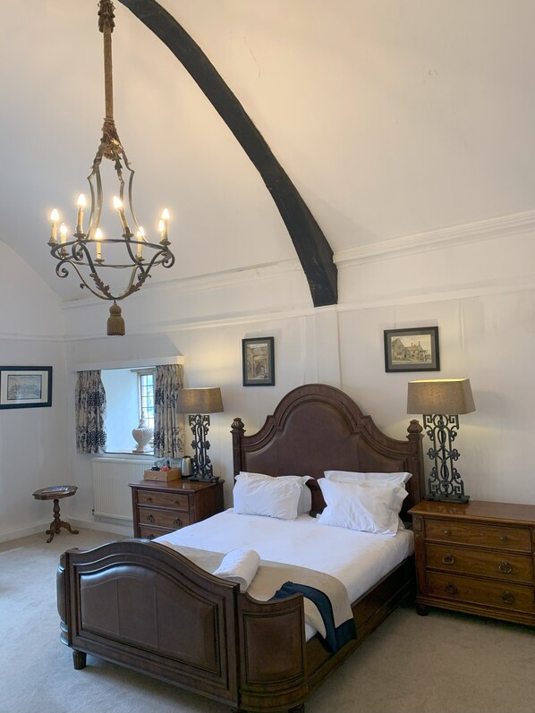 Quarto com uma cama grande, um candelabro, duas mesas de cabeceira com luminárias, cômoda e uma janela com cortinas.