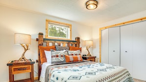 Quarto com cabeceira de madeira, duas mesas de cabeceira com luminárias, cama com roupa de cama estampada, uma janela e um guarda-roupa.