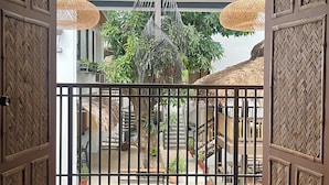 Quarto com vista para um pátio, com tapete de piso estampado, luminária trançada pendente e portão de metal.