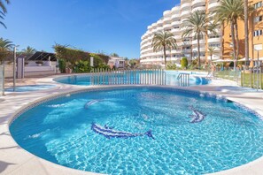 Uma piscina com borda decorativa, cercada por uma grade, e adjacente a um edifício com várias varandas.