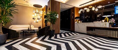 Um lobby moderno com piso em padrão geométrico preto e branco estilo Chevron, um balcão de recepção e uma área de estar com sofá e mesa de centro.