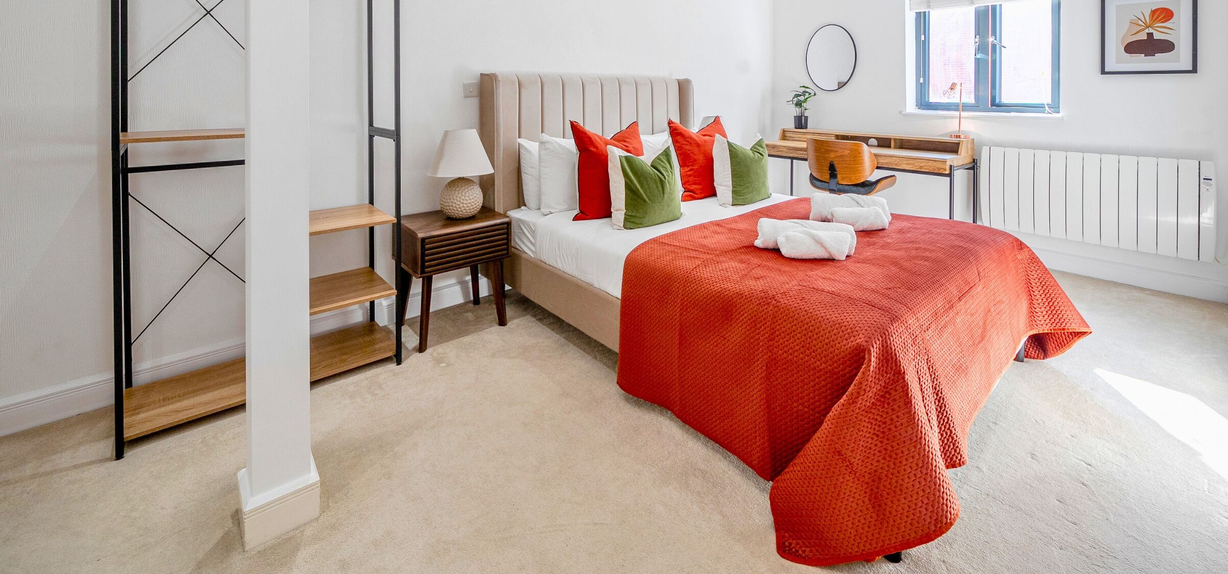 Quarto bem arrumado com cama, almofadas, mesa de cabeceira, abajur, cadeira e radiador.