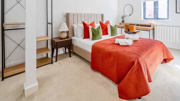 Quarto bem arrumado com cama, almofadas, mesa de cabeceira, abajur, cadeira e radiador.