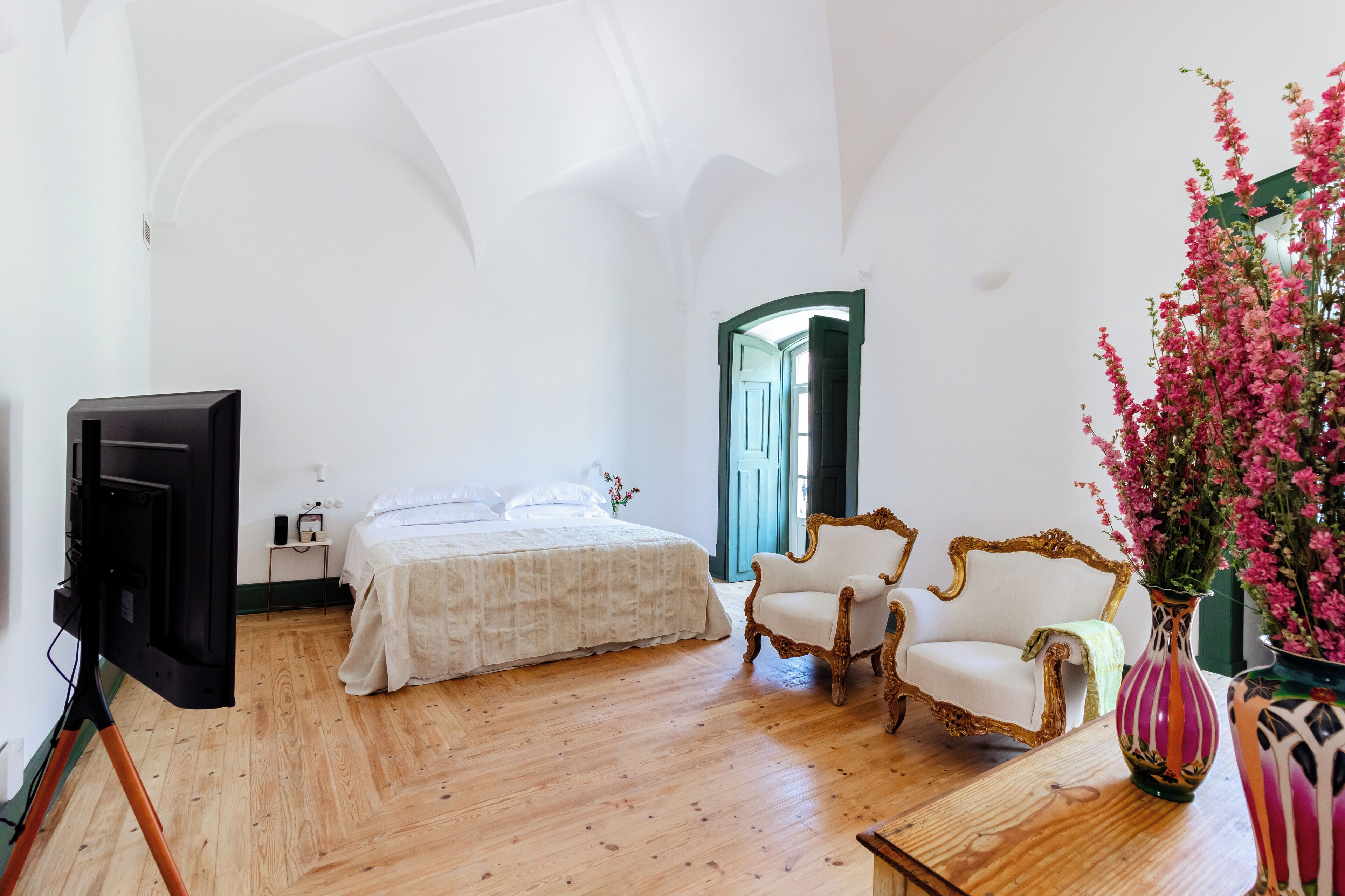 Quarto com cama, televisão, cadeira e um vaso com flores.