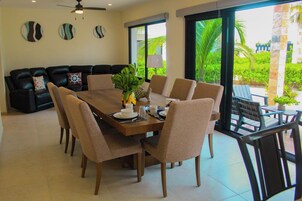 Uma área de refeições com mesa de madeira, cadeiras bege e um vaso de planta.