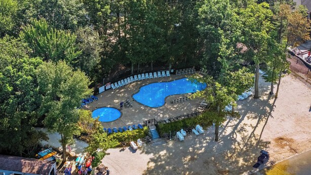 Vista aérea de um resort com duas piscinas, cadeiras de lounge ao redor e um edifício com caiaques.