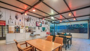 Um restaurante com área de refeições de madeira, paredes brancas e decorações penduradas, e um refrigerador Coca-Cola.