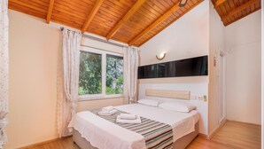 Quarto com teto de madeira, uma janela grande com cortinas, cama com cobertor listrado e televisão na parede.