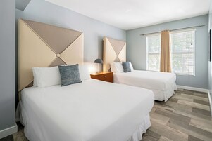 Quarto de hotel com duas camas, uma mesa de cabeceira e uma janela com persianas.