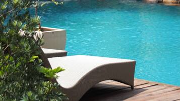 Área de piscina com espreguiçadeiras e deck de madeira.