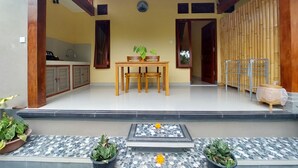 Uma sala de jantar com mesa e cadeiras de madeira, uma cozinha ao fundo e uma planta decorativa em primeiro plano.