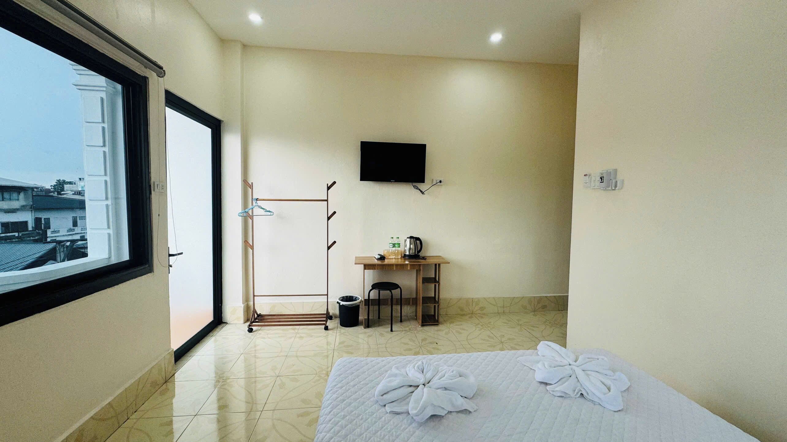 Quarto de hotel com cama, escrivaninha, televisão, janela e vista para edifícios.